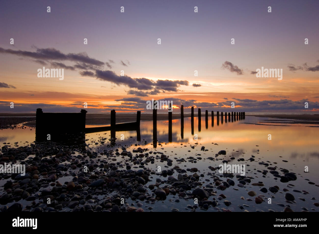 beach and wooden groyne at sunset with large pools of water and cloud ...