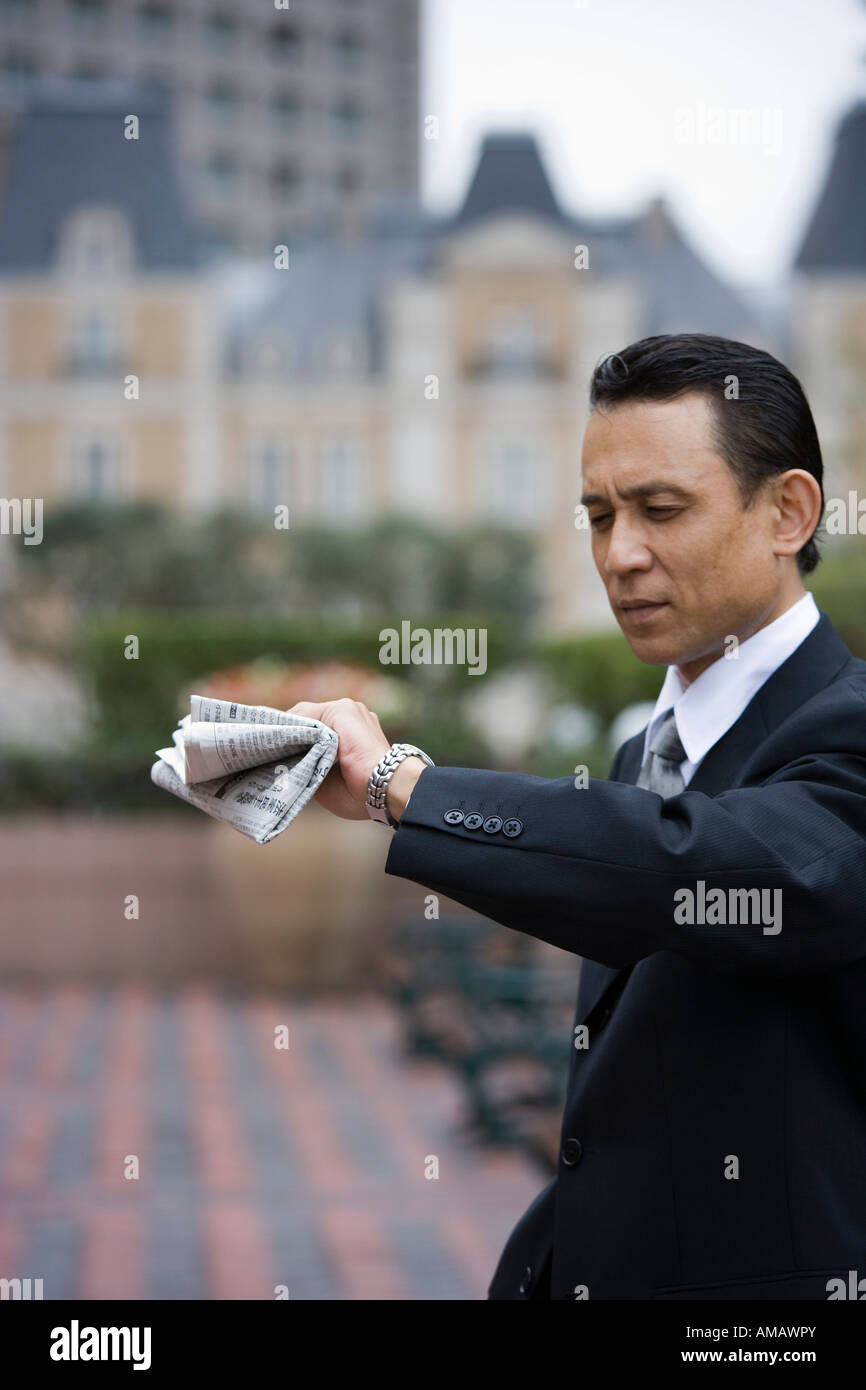 A businessman carrying a newspaper and looking at his watch Stock Photo ...