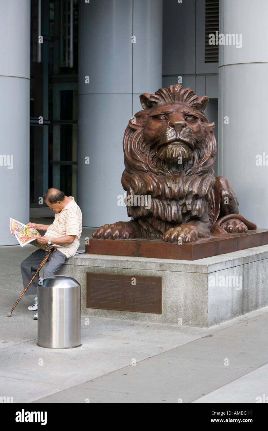 A man reads his newspaper by one of the bronze lion statues in front of ...