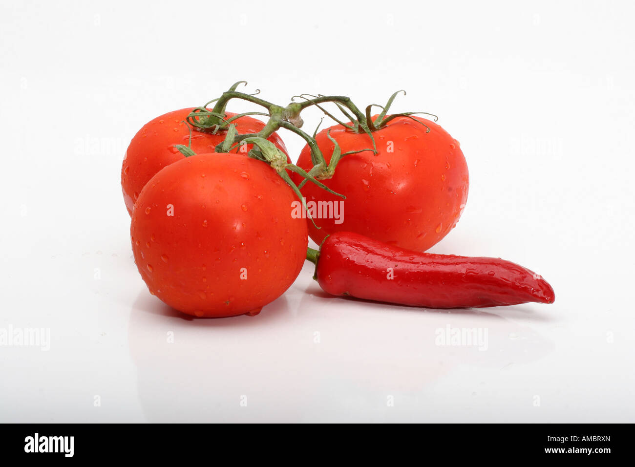 Ripe red cherry tomatoes on the stems and chillie pepper with drops of water on white background ...