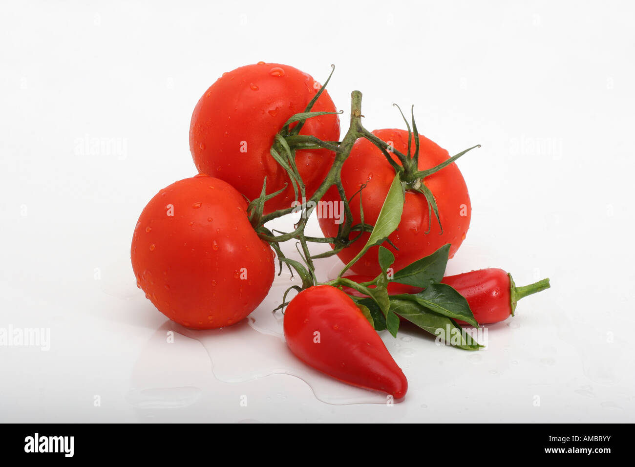 Ripe red cherry tomatoes on the stems and chillie peppers with drops of water on white ...