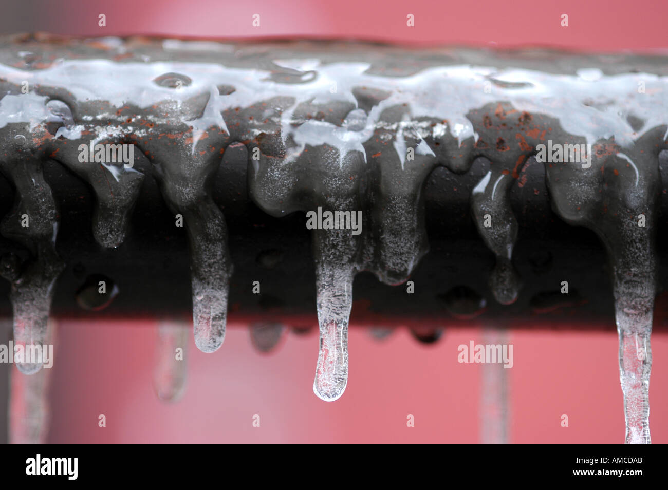 Ice hanging icicles on horizontal black pole red bkgrnd background ...