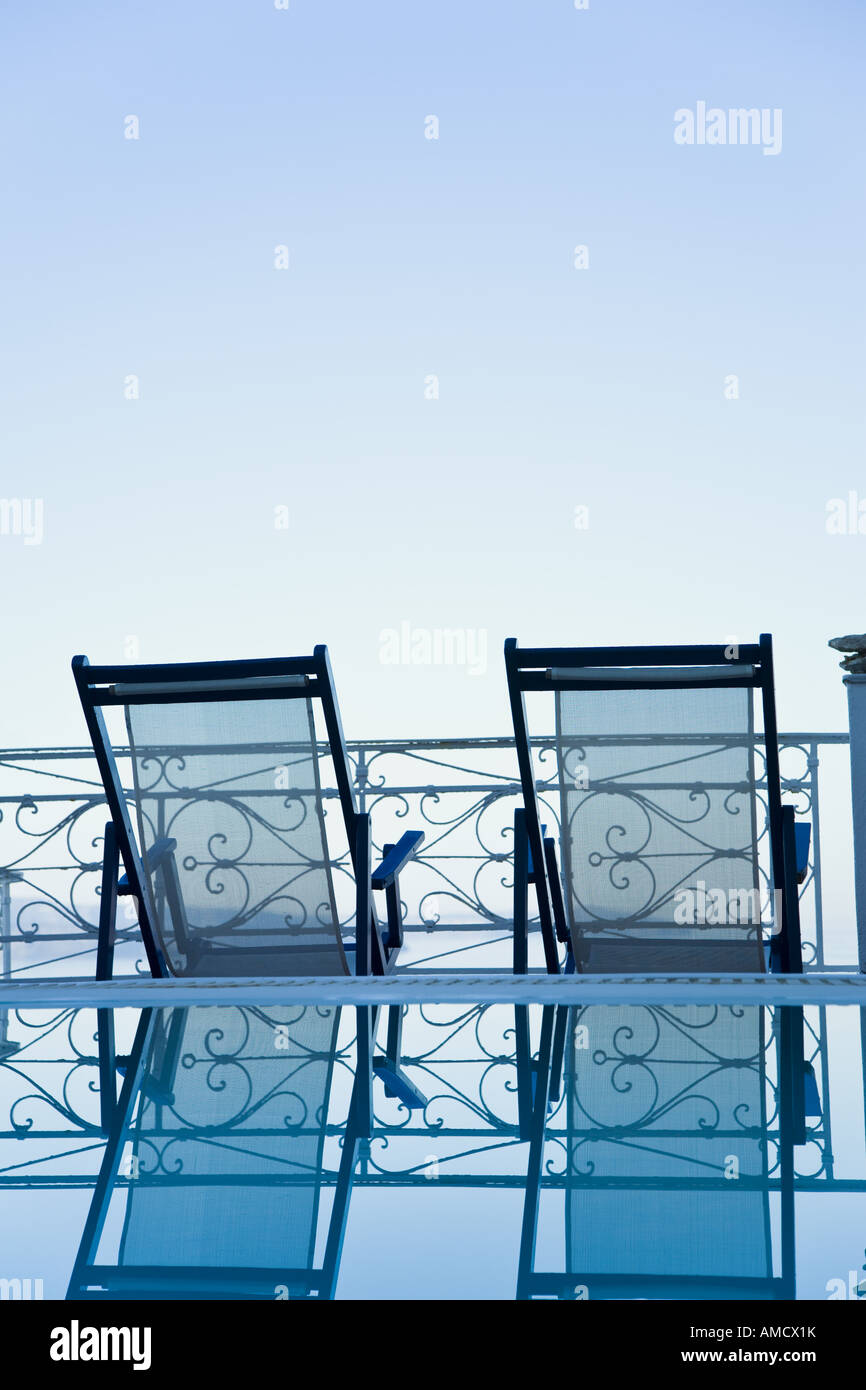 Rear view of two empty deck chairs and pool with reflection Stock Photo ...