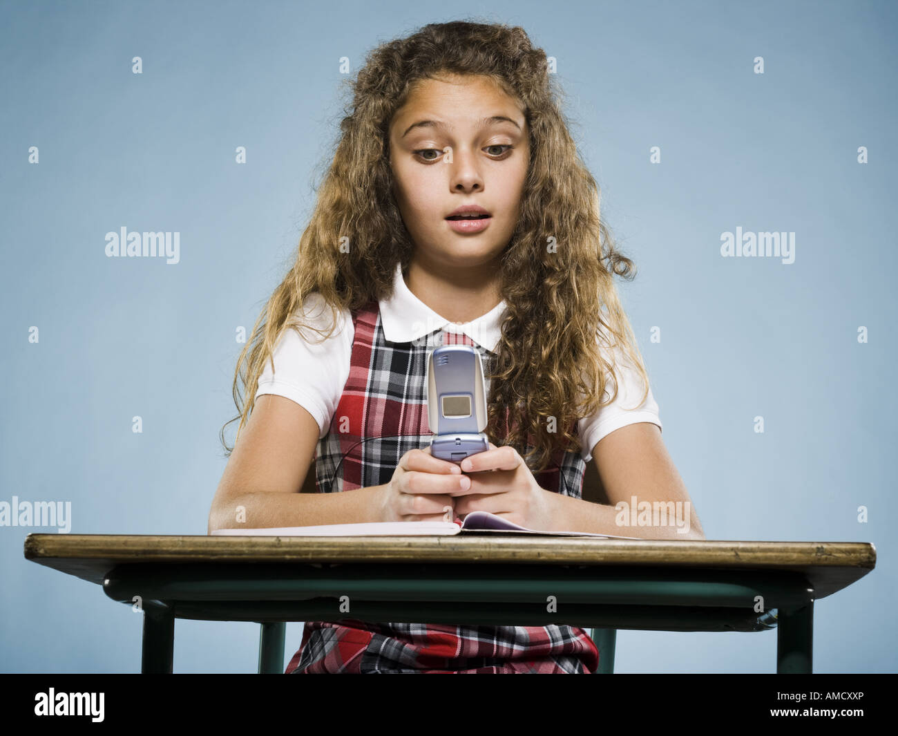Girl sitting at desk with workbook and cell phone Stock Photo - Alamy