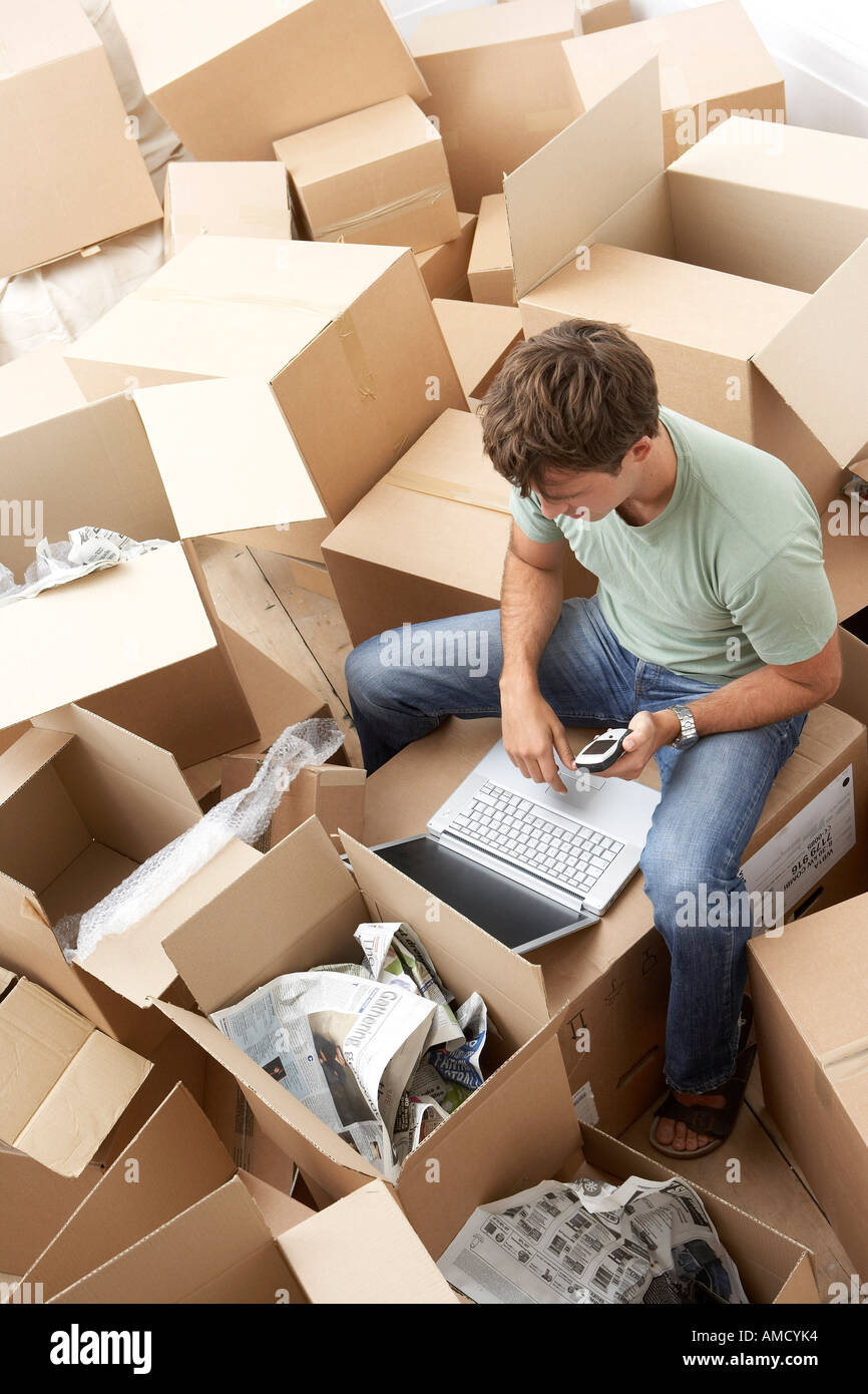 Man Sitting amongst Moving Boxes with Laptop Computer and Cellular ...