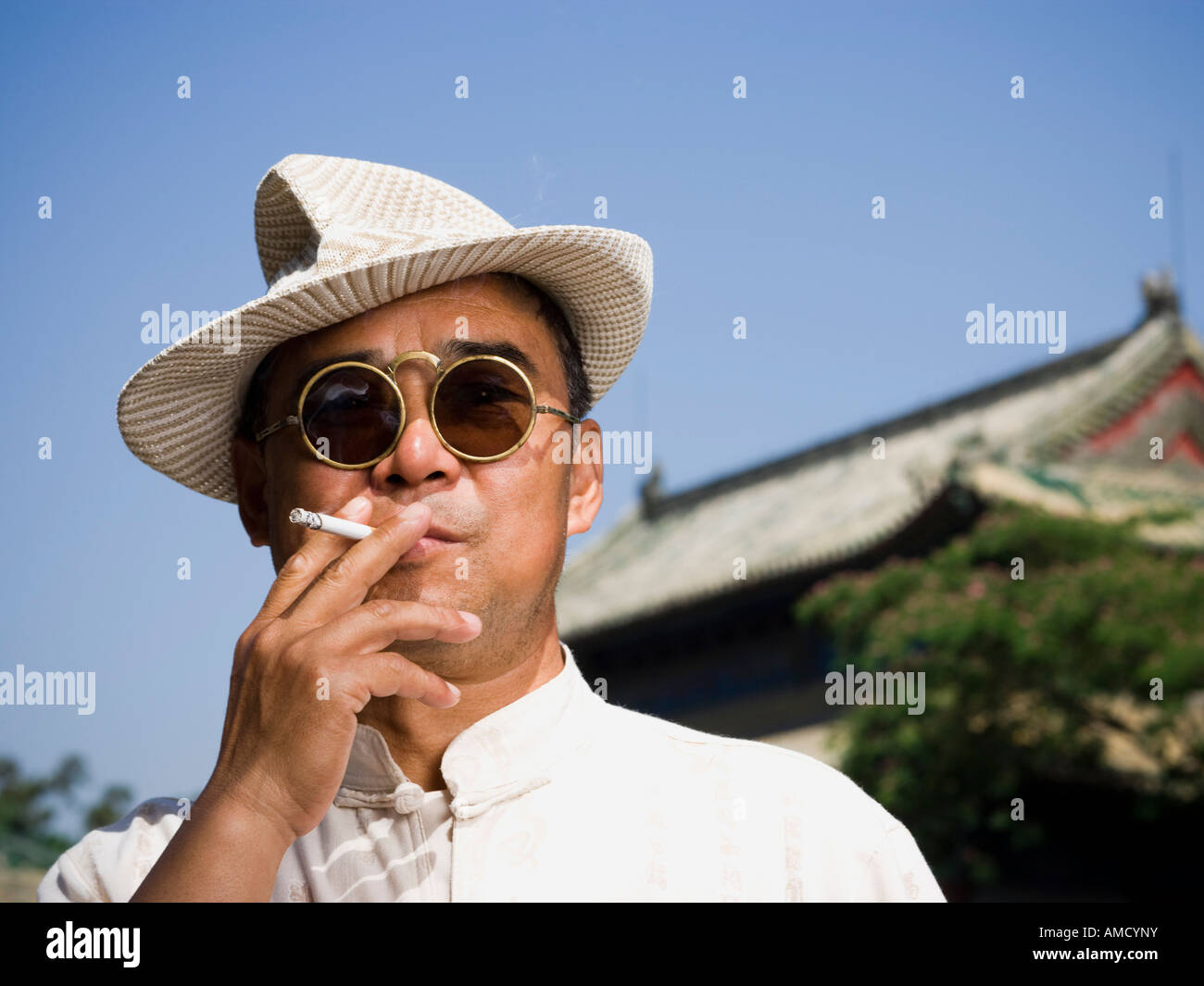 Man with sunglasses and straw hat smoking cigarette outdoors with ...