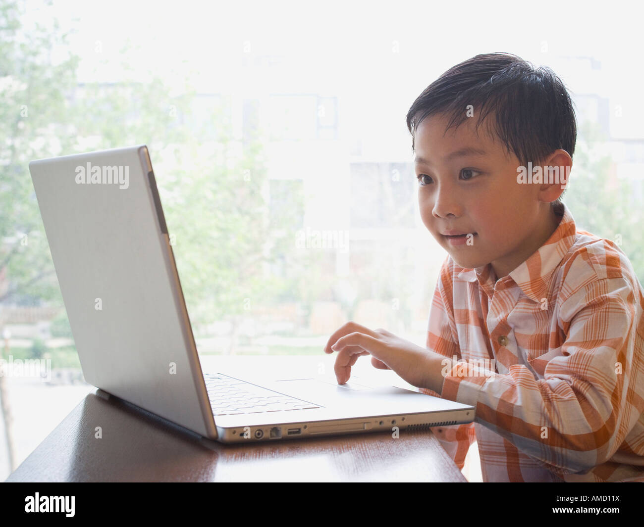 Boy sitting with laptop in front of large window smiling Stock Photo ...