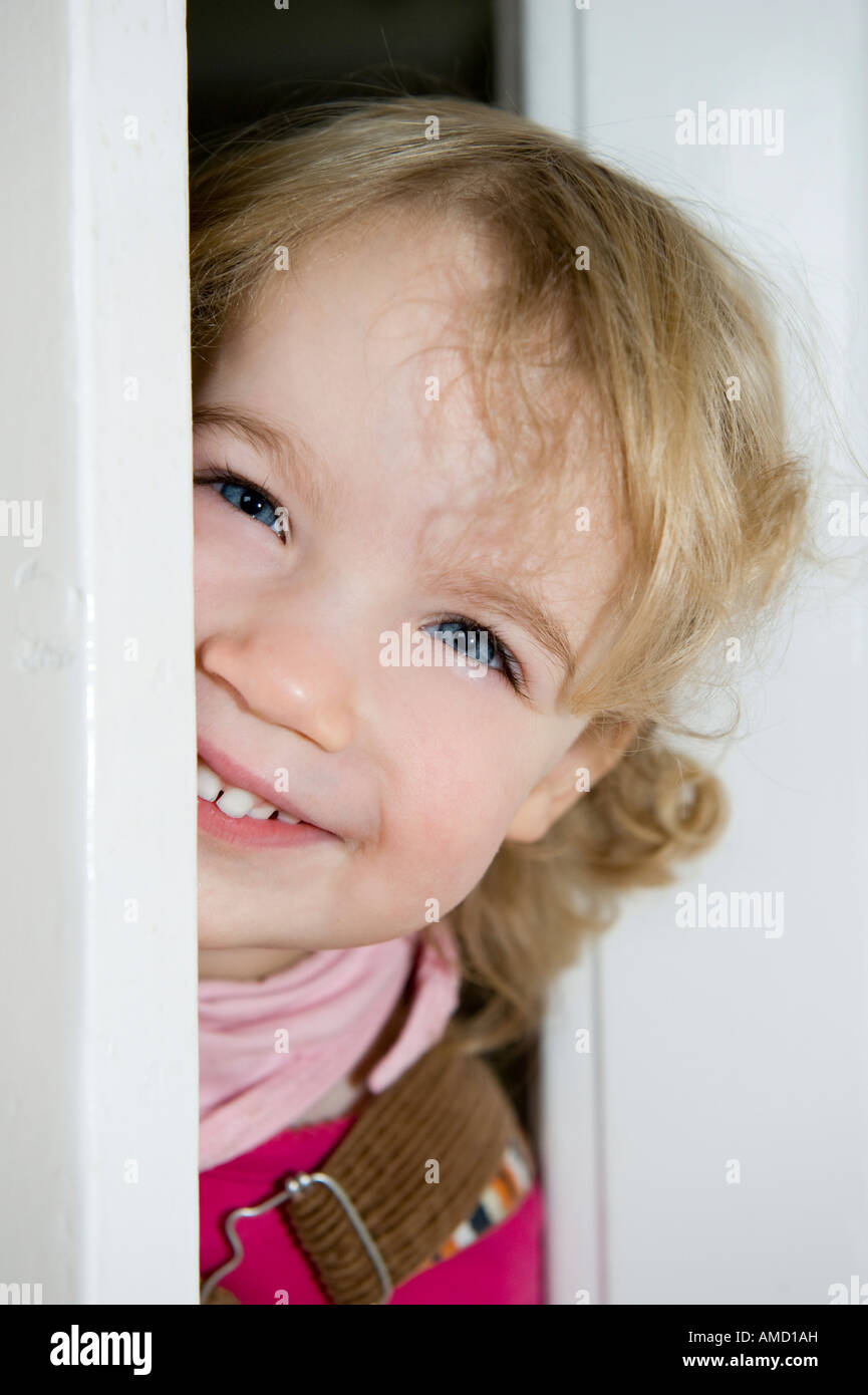 Smiling young girl behind a door Stock Photo - Alamy