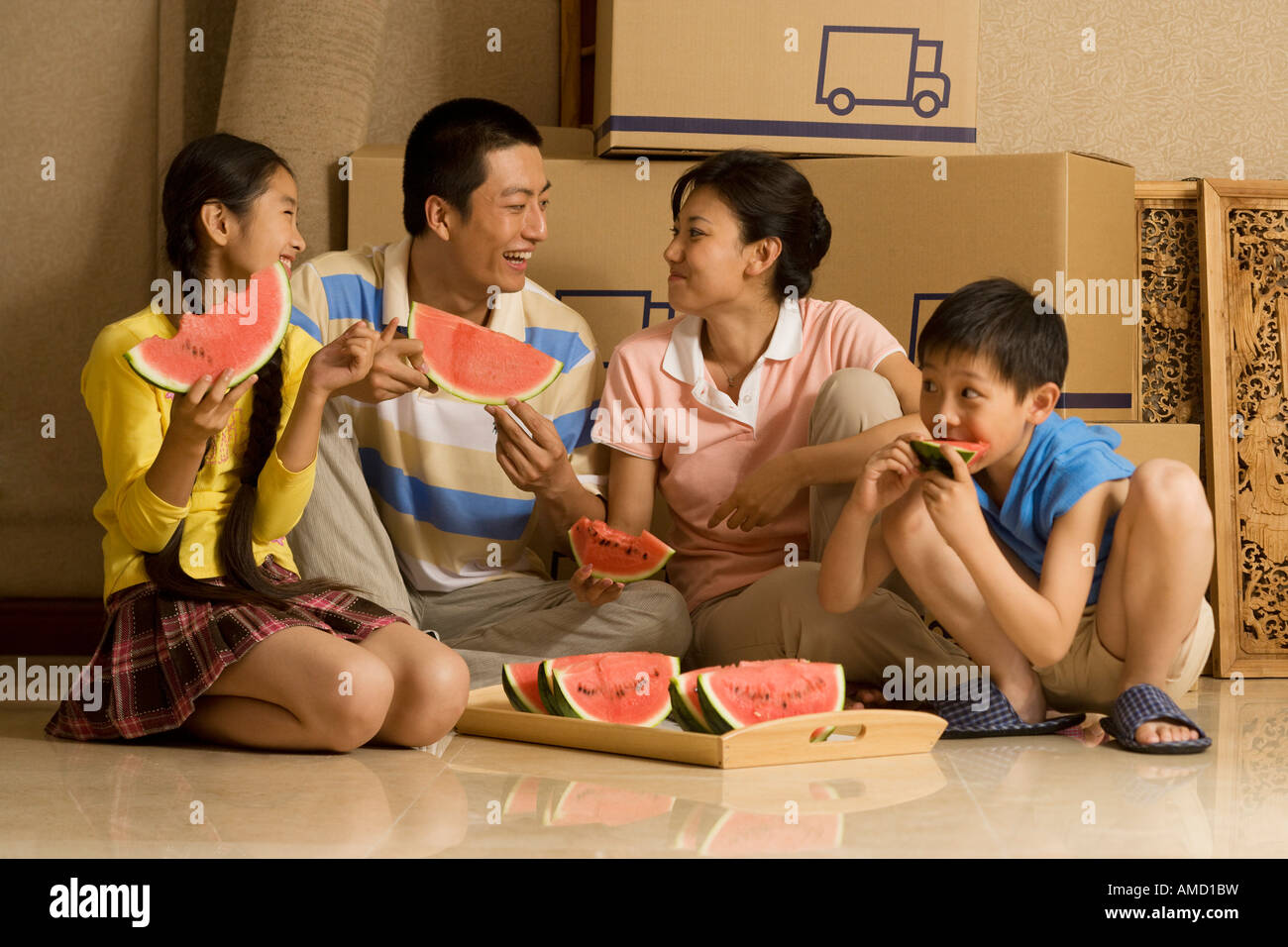 Family of four eating watermelon and smiling with cardboard boxes in ...