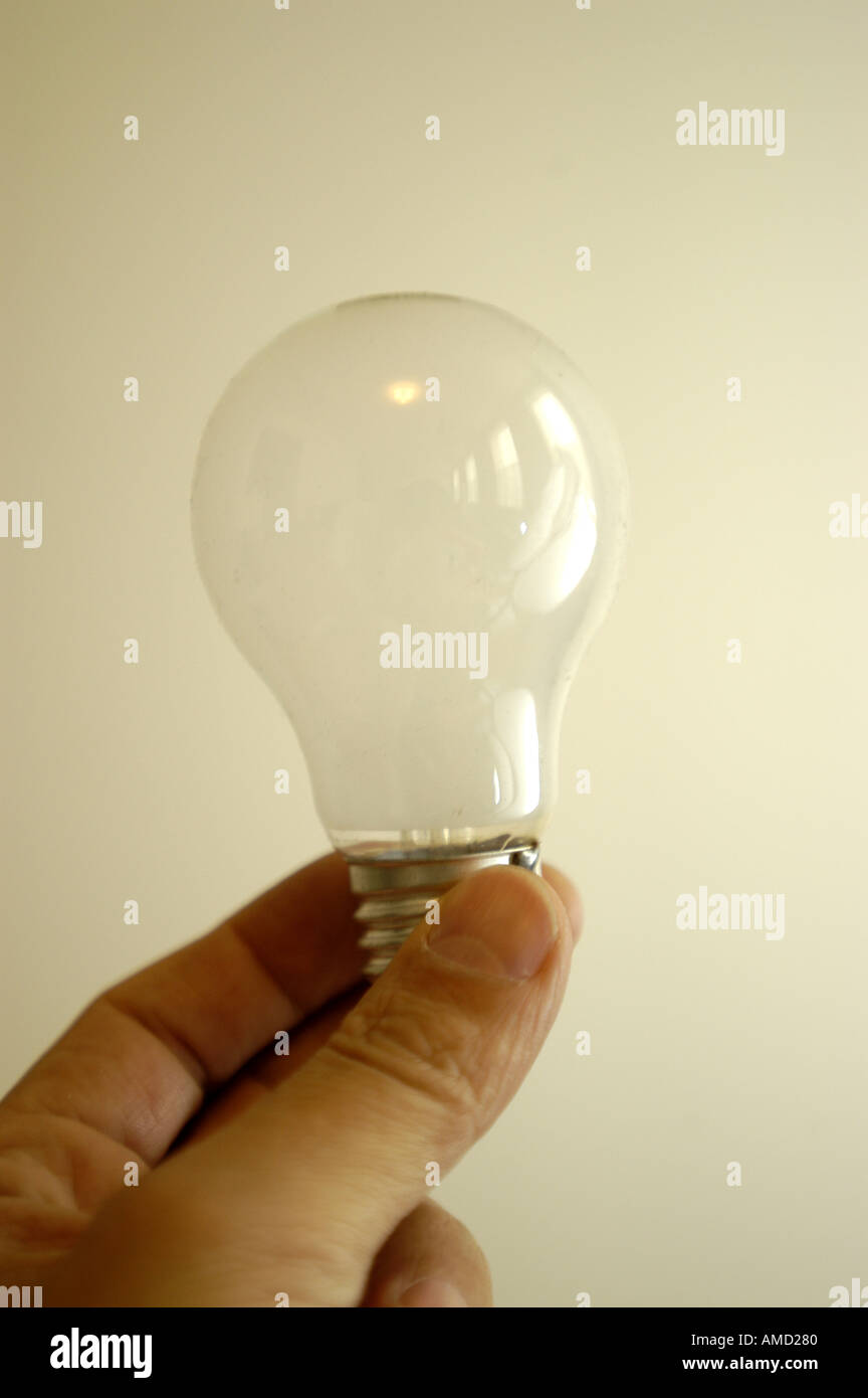 Thumb and forefinger holding light bulb slightly tilted left cream ...