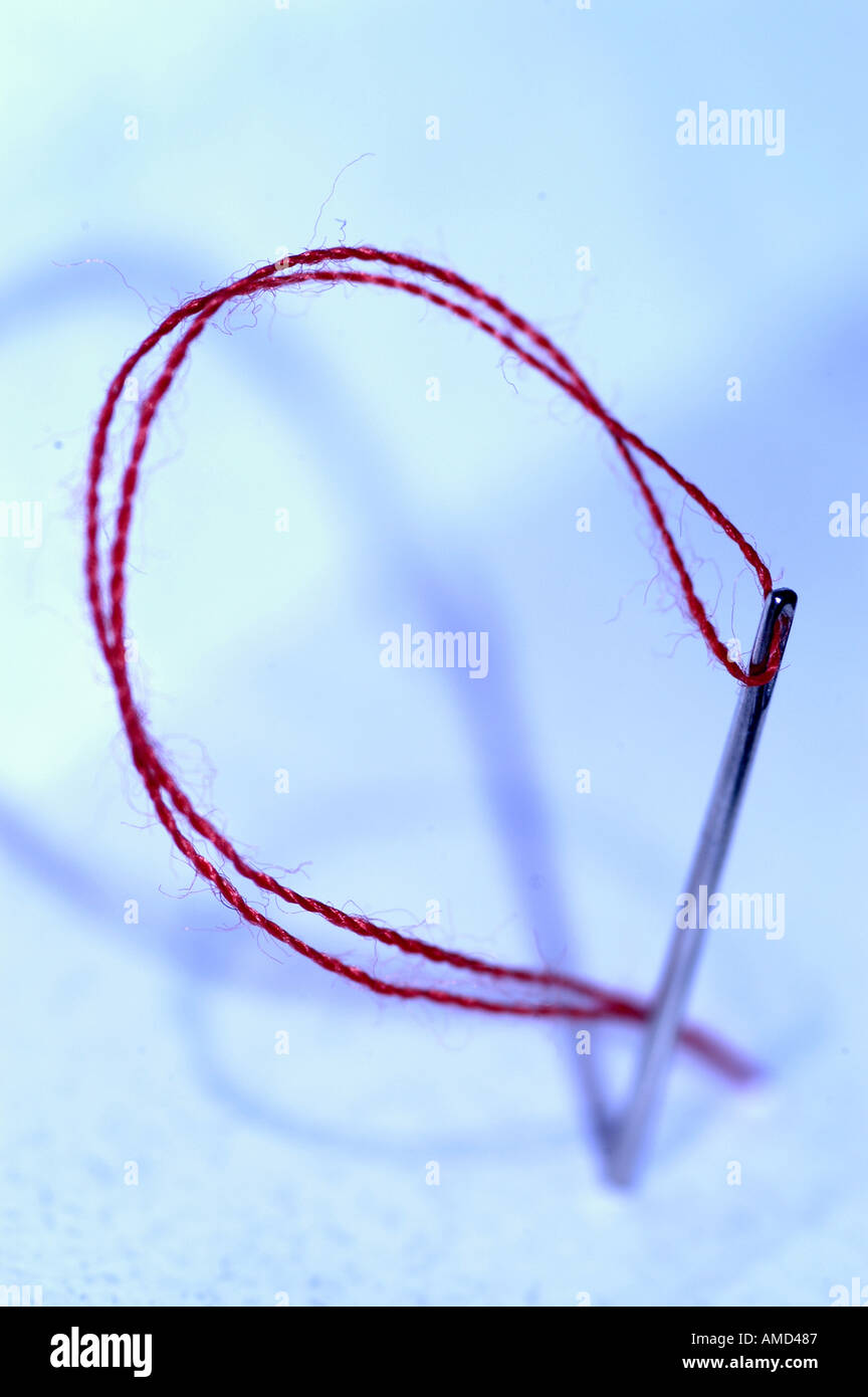 Needle w red thread looped stuck upright in white top side view blue ...