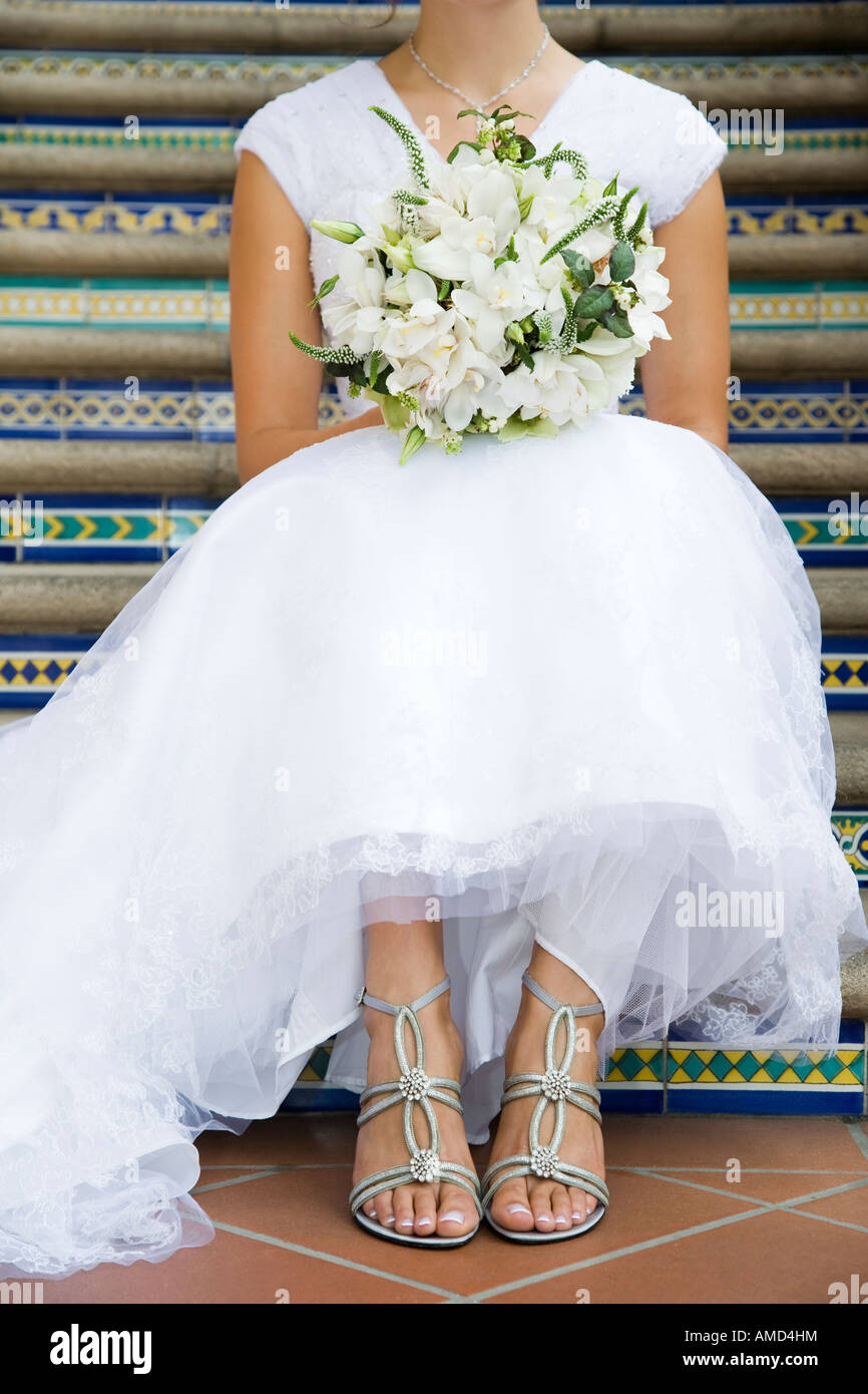Bride sitting on steps with bouquet neck down Stock Photo - Alamy