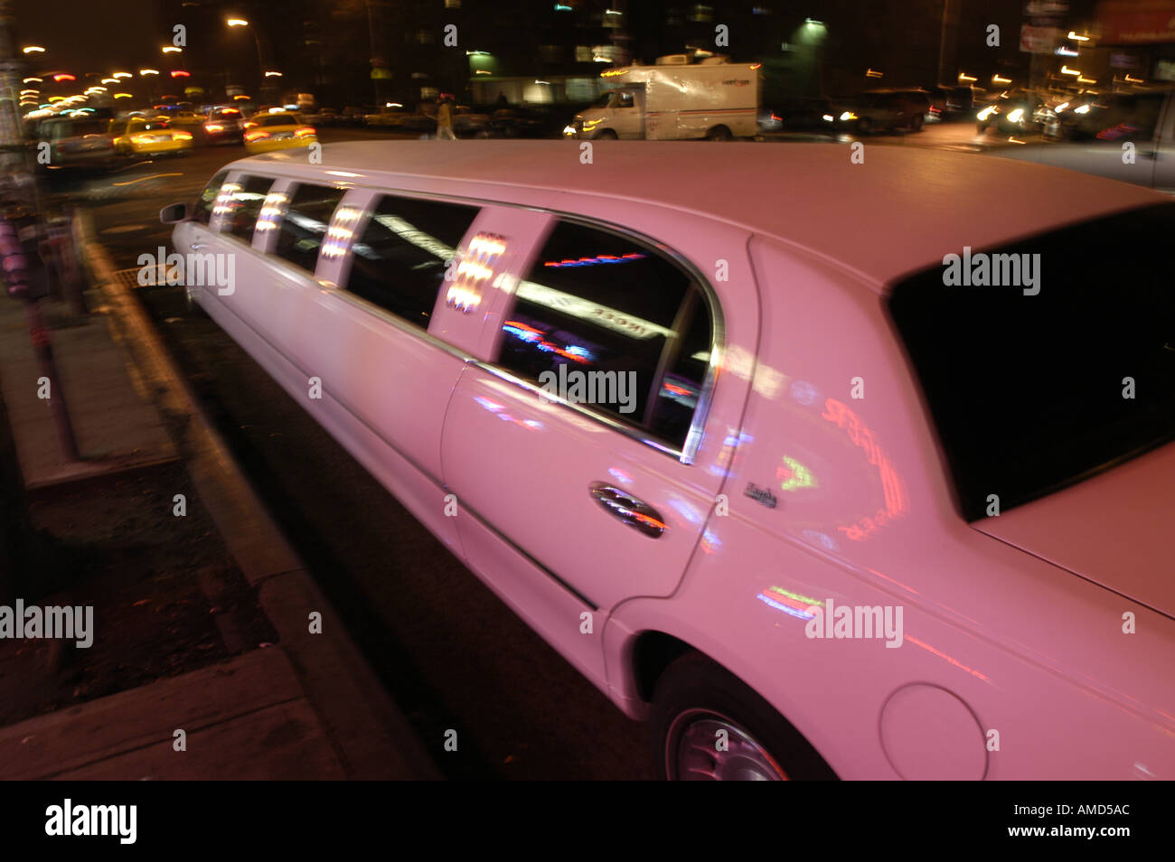 White limousine under pink lights from left rear city lights bkgrnd ...
