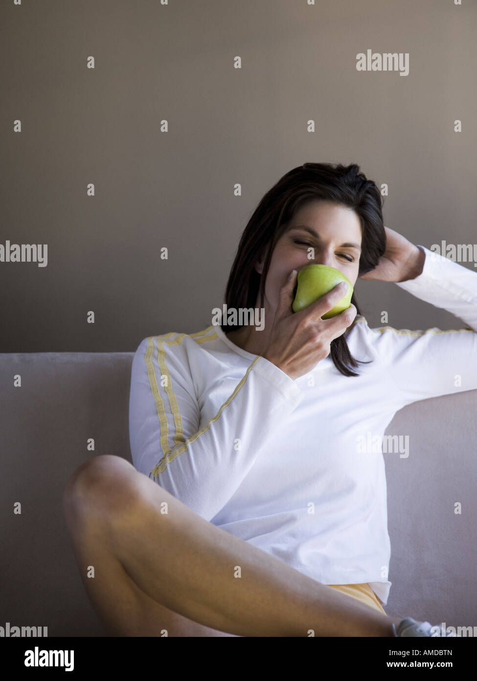 Woman sitting on sofa eating green apple Stock Photo - Alamy