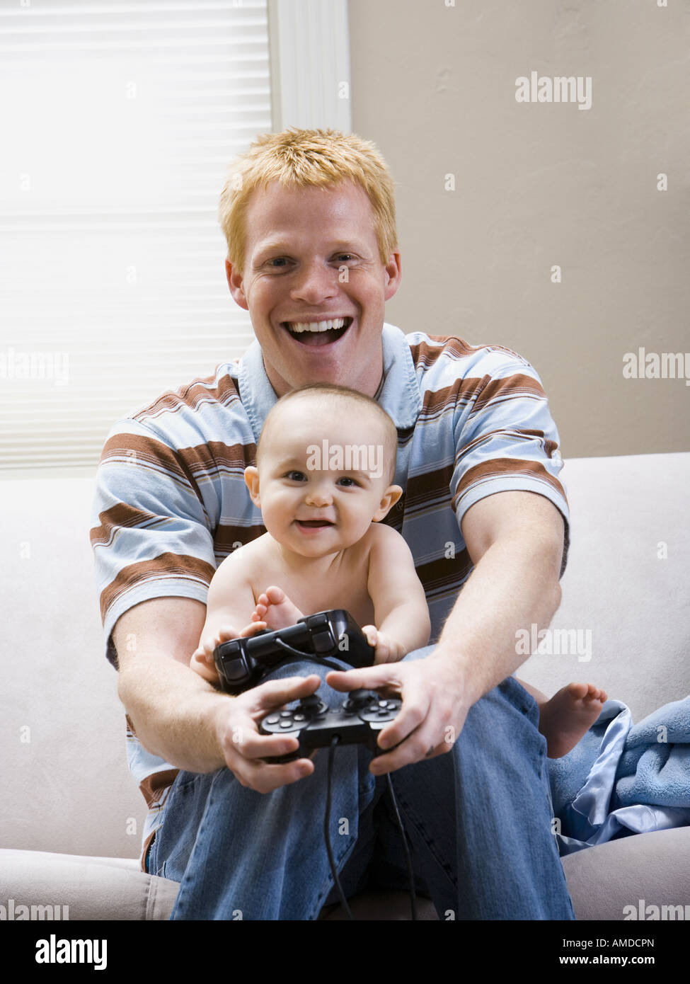 Man and baby on sofa with video game controller smiling Stock Photo - Alamy