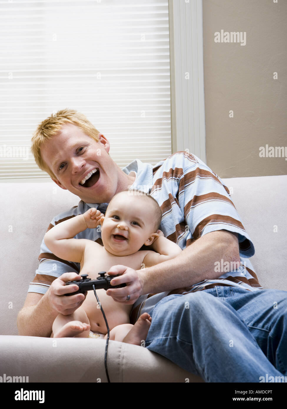 Man and baby on sofa with video game controller smiling Stock Photo - Alamy