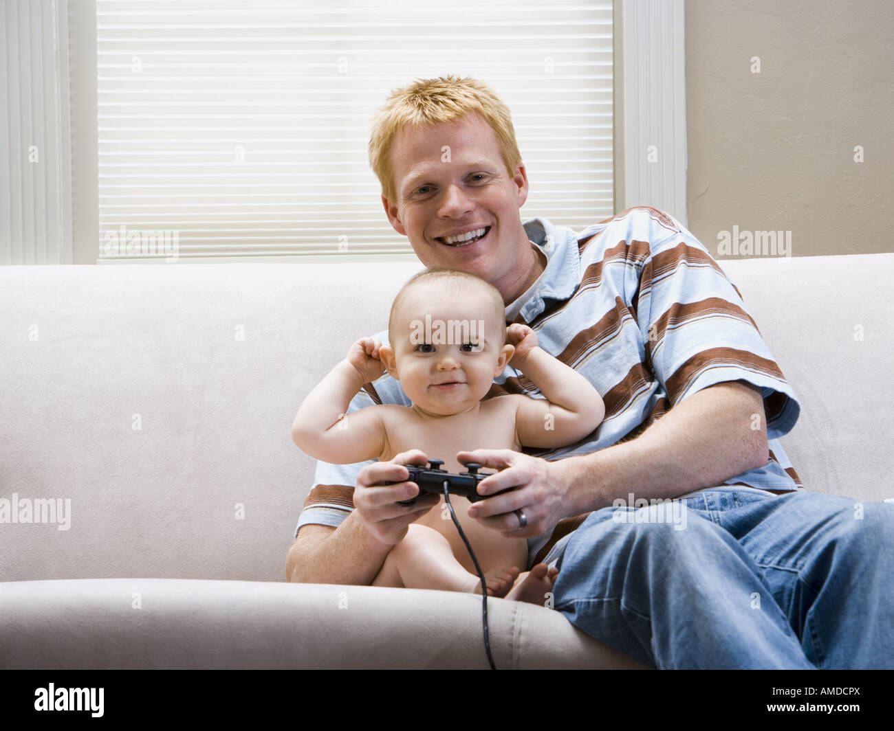 Man and baby on sofa with video game controller smiling Stock Photo - Alamy