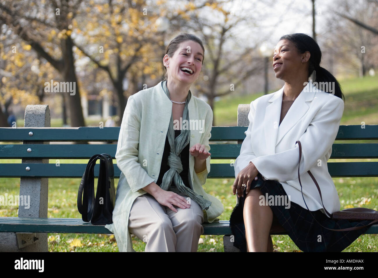 Two women sitting on a bench in the park and laughing Stock Photo - Alamy