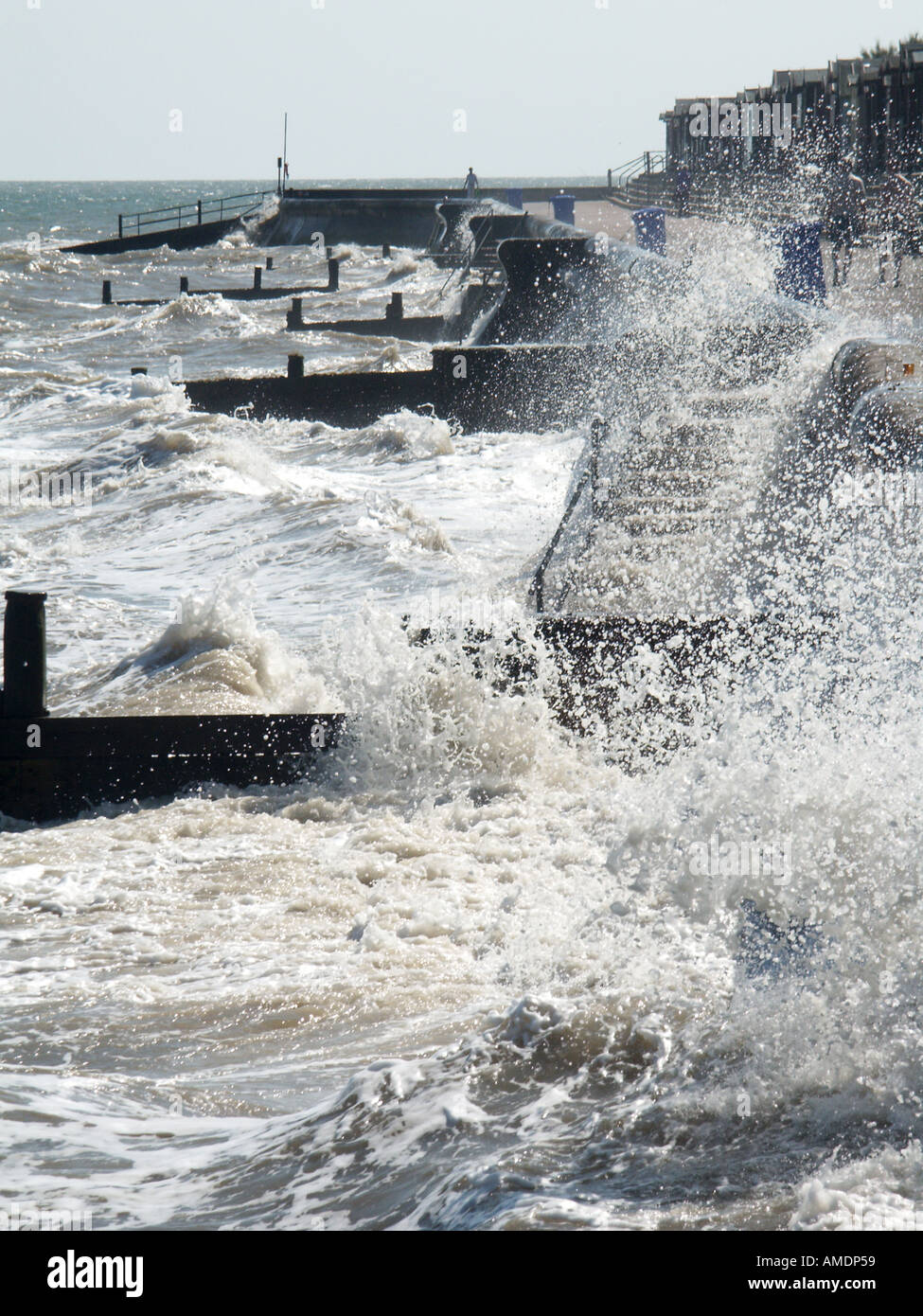 People walking in sea spray along concrete sea wall & promenade windy ...