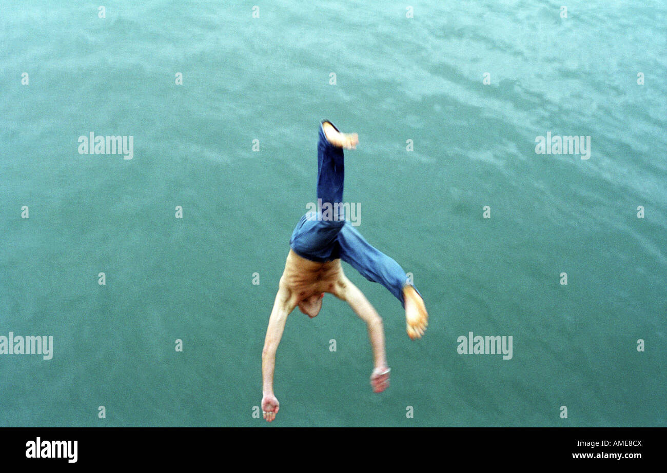 Unidentifiable, faceless, shirtless man jumps off a pier into blue ...
