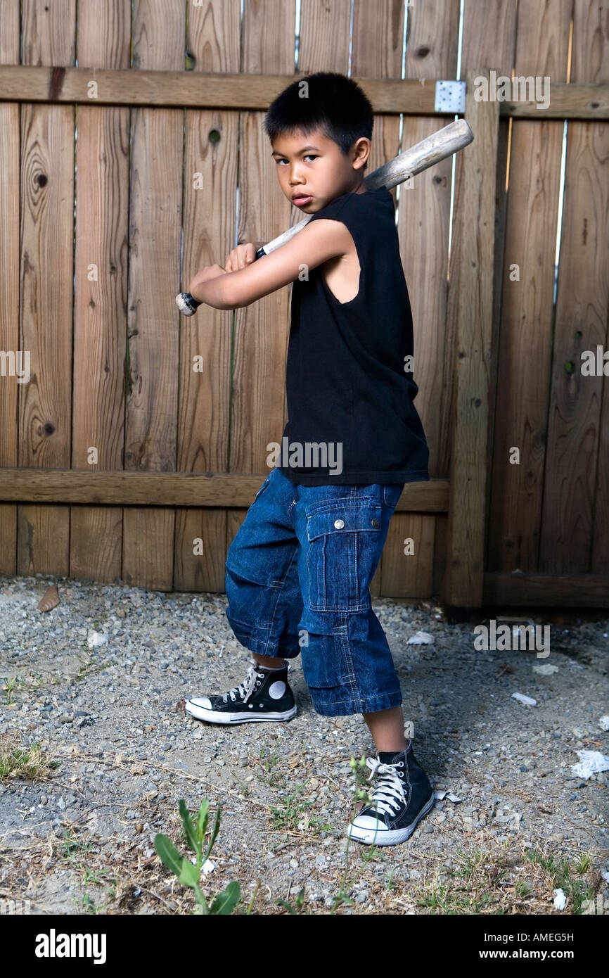 Young asian boy standing outside beside a tall wooden fence wearing ...