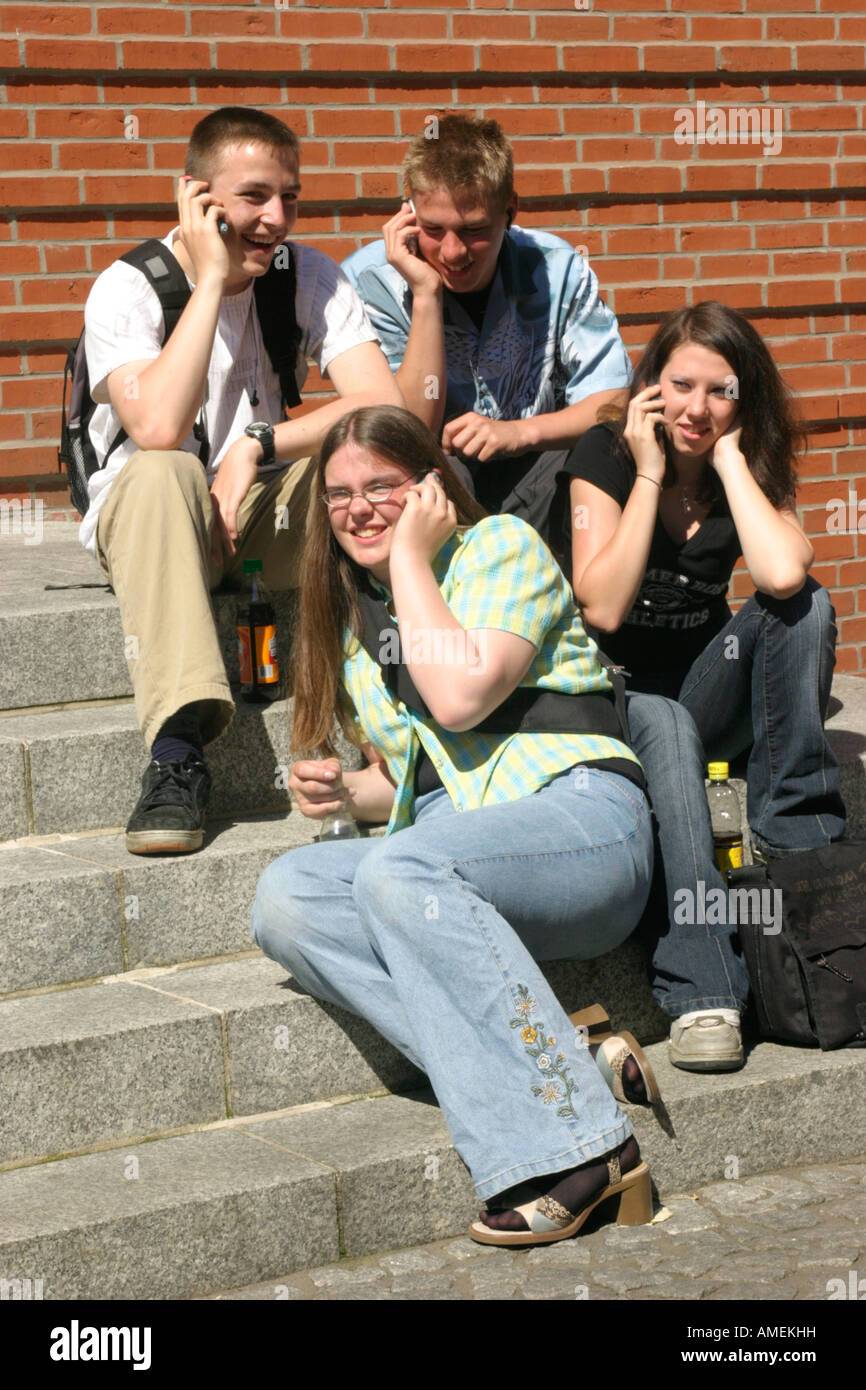four teenagers talking on their mobile phones sitting on stairs in town ...