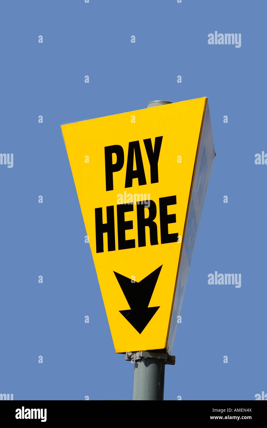 Yellow pay here sign with black text and arrow against a clear blue sky ...
