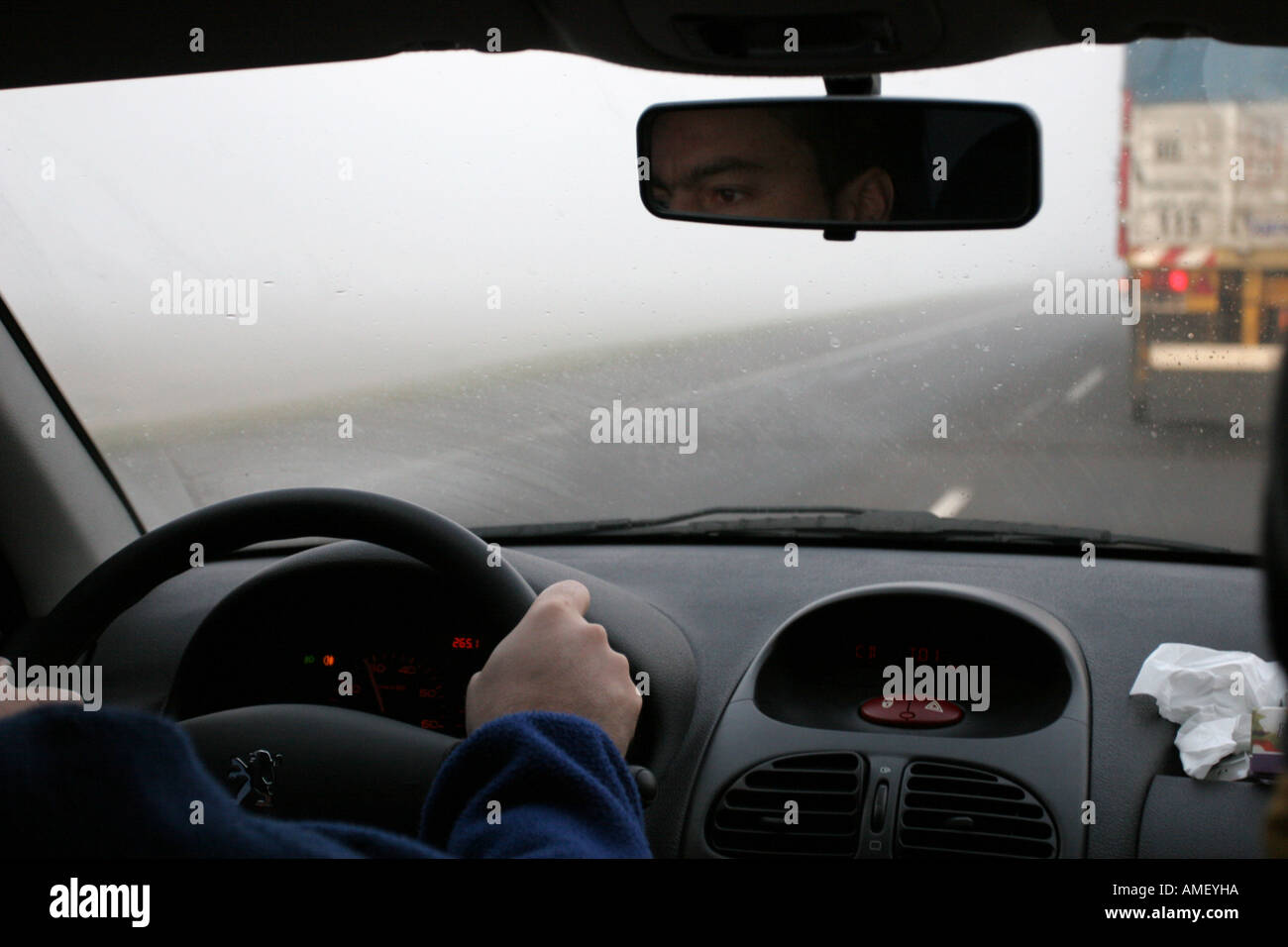Man driving a car in a misty road behind a truck. View from the inside ...