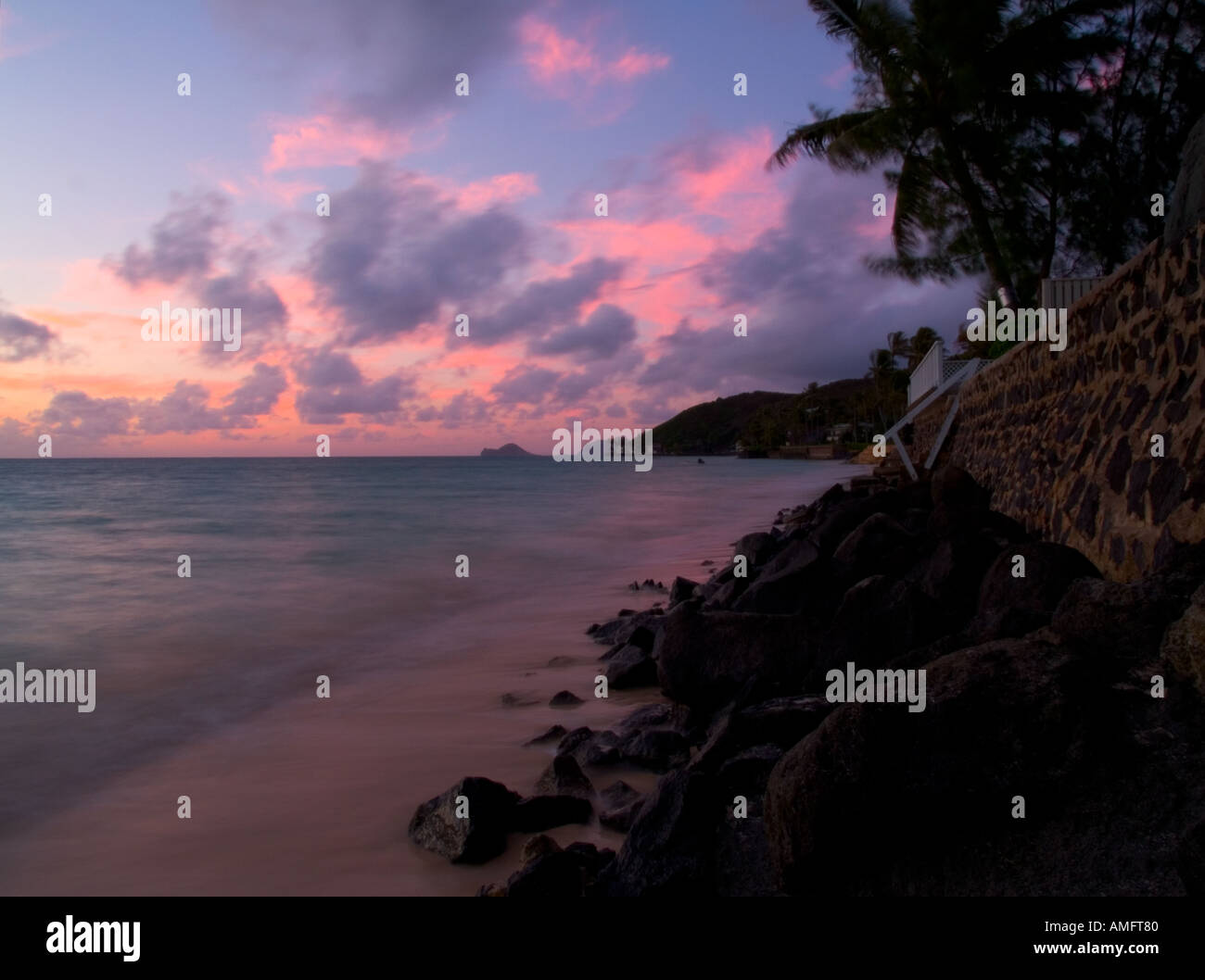 The beautiful pink glow of the morning sun rising over a beach in Oahu ...