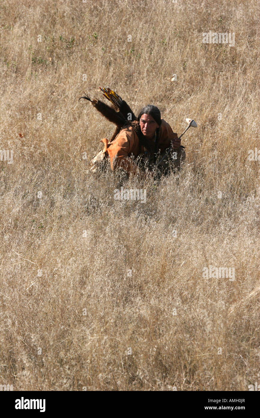 A Native American Indian man crouching in the dead grasses hunting game ...