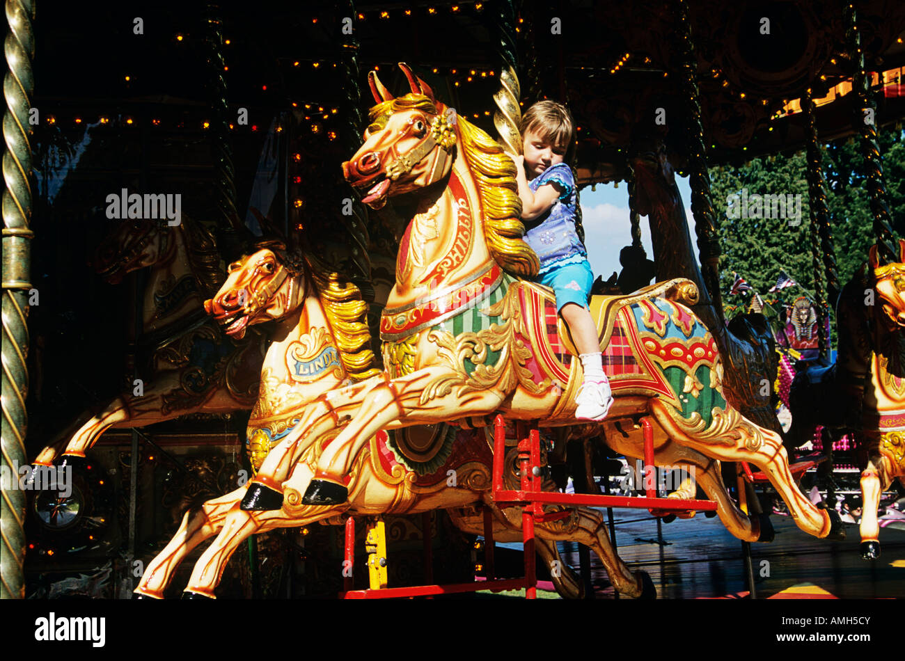 Child riding on colourful painted horse on fairground carousel, England ...