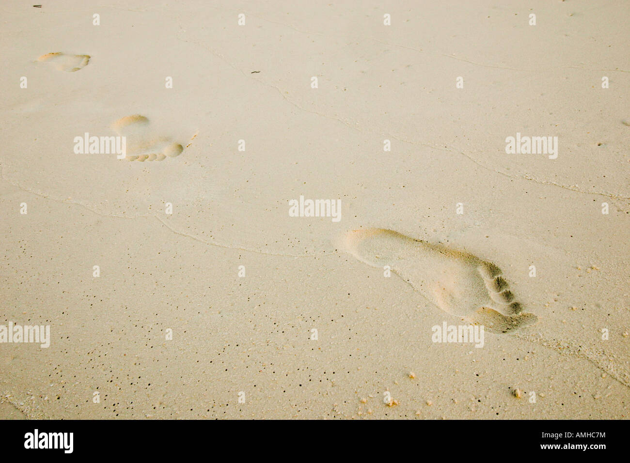 Three footprint on a beach lead towards the camera filling the diagonal ...