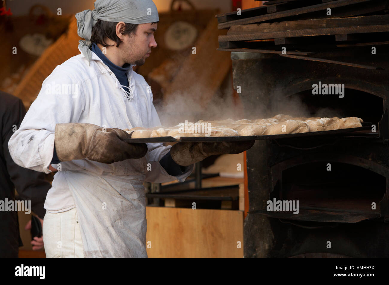 Baker removing tray of bread with steam rising from an outdoor wooden ...
