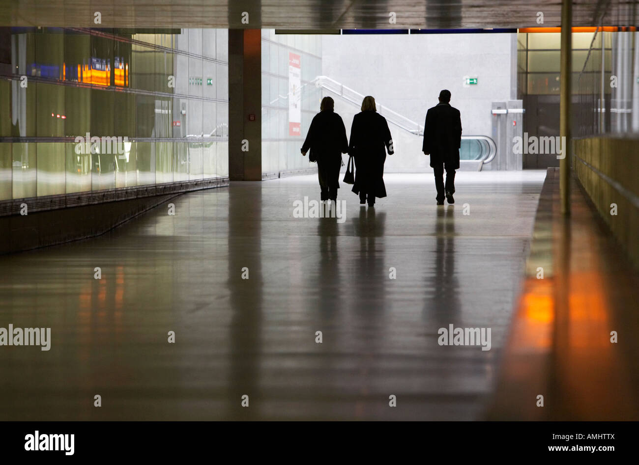 man and two women walking along underground walkway towards light ...