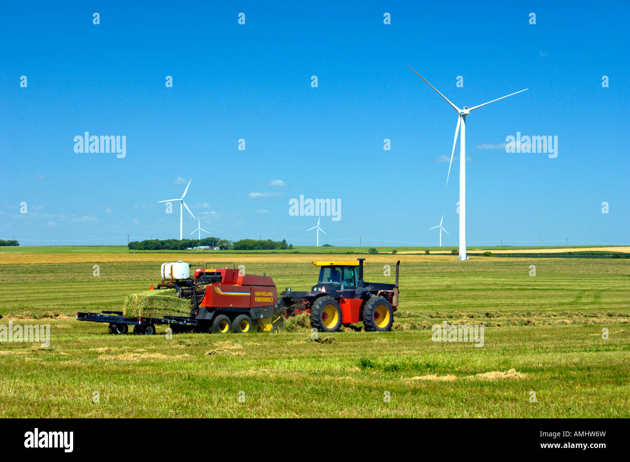 Electrical windfarm windmills and hay baling equipment on a field near ...