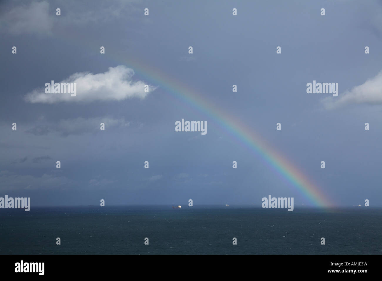 A vivid rainbow arching over a dark blue ocean with cloudy sky and ...