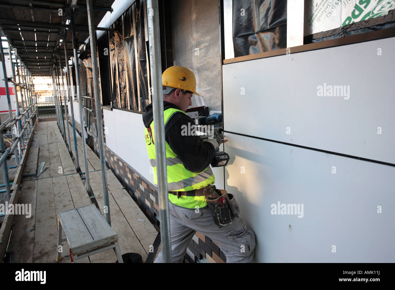 A migrant worker from Lithuania securing cladding to a wall on a ...