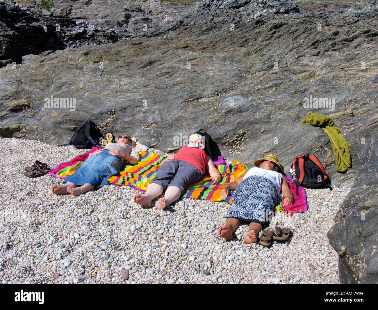 3 middle-aged women asleep in the sun on a pebbly beach South Devon, UK ...