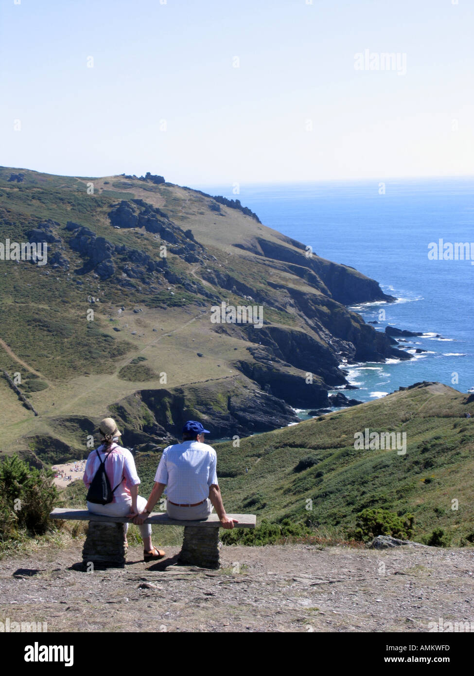Walkers resting on a bench on a spectacular coastal path overlooking ...