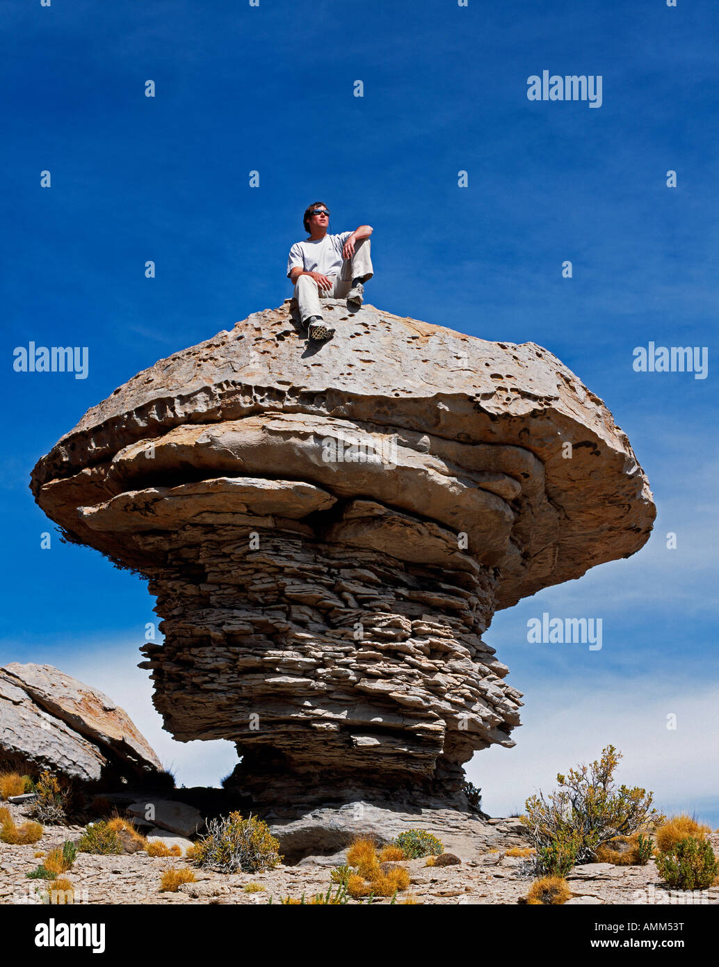 A tourist sits on top of a massive wind-eroded boulder that rises above ...