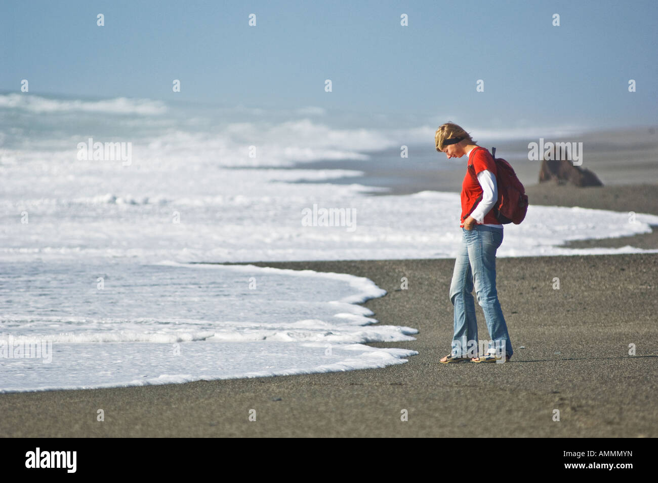 Single female watches approaching tide on empty west coast beach on the ...