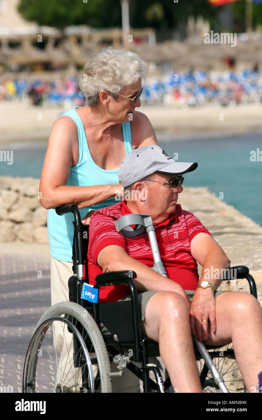 Woman pushing old man with blue hat and walking stick in wheelchair on ...