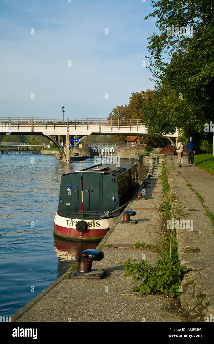 Narrow boat moored on towpath below the River Thames weir and road ...