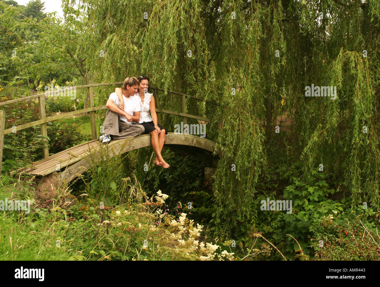 Couple on a small arched wooden bridge in garden surrounded by lush ...