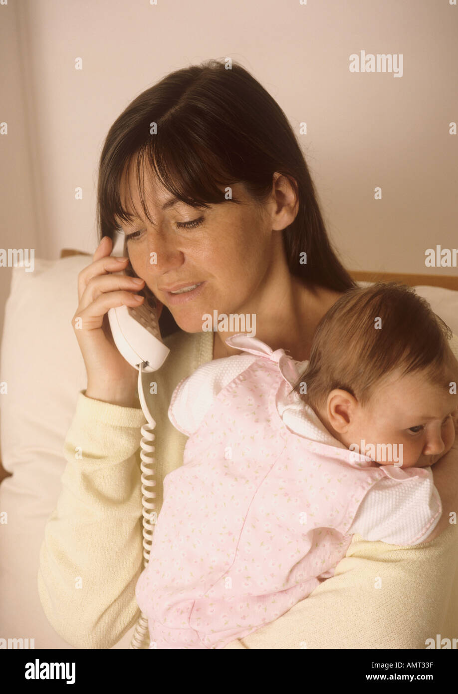 Worried looking mother with her baby girl using a telephone to call ...