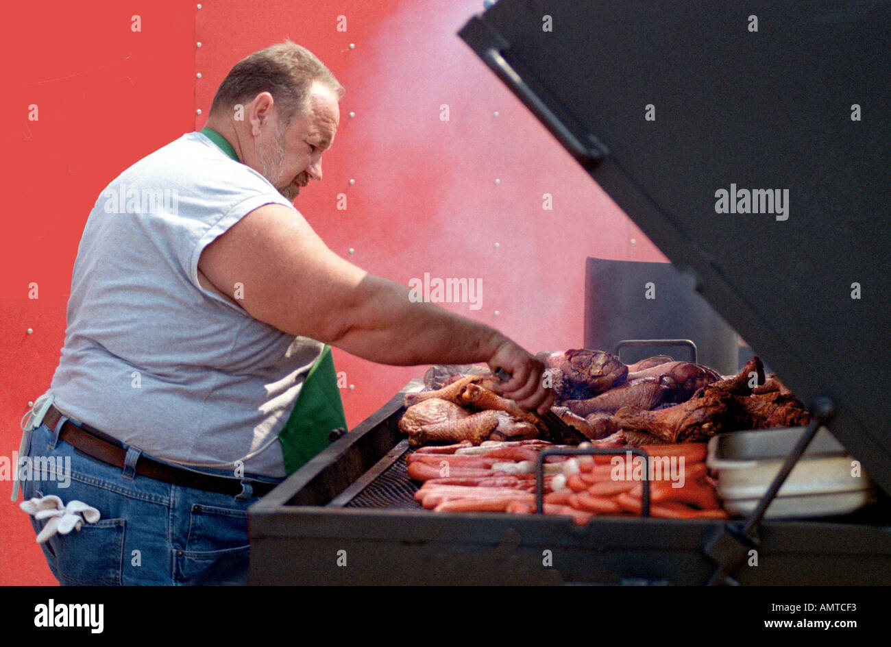 Overweight adult male cooks on a barbeque for a large group of people ...