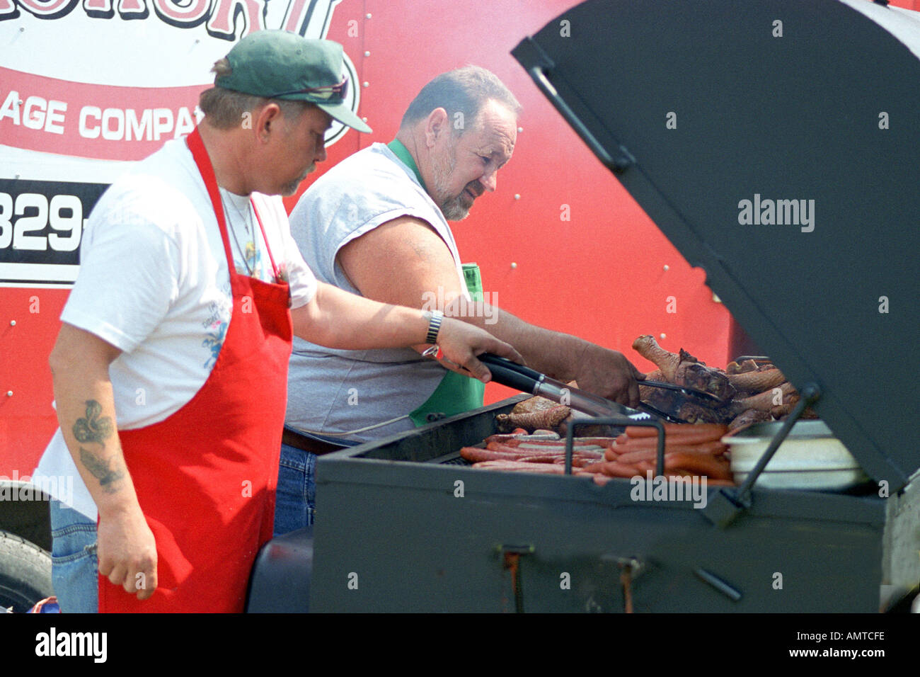 Overweight adult male cooks on a barbeque for a large group of people ...