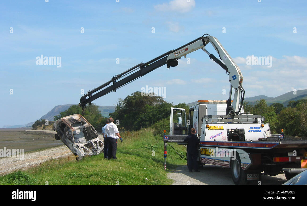Burnt out car abandoned on welsh beach, being removed by crane Stock ...