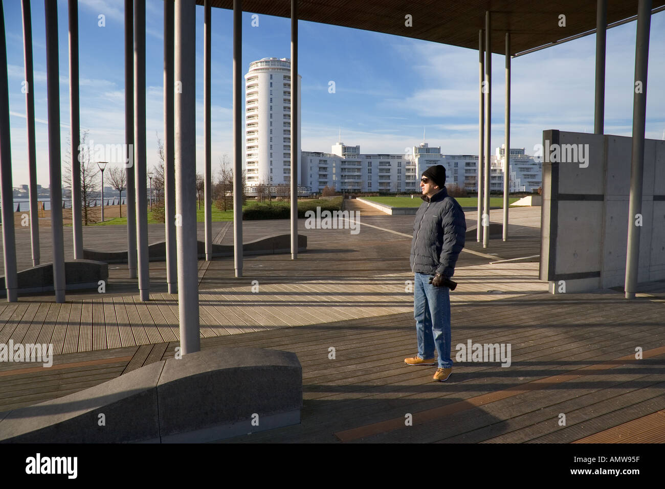 Man standing on decking looking into bright sunshine with apartment ...