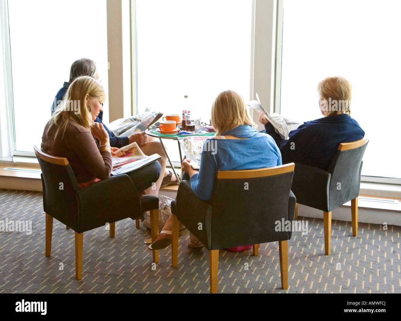 Four people reading newspapers and magazines at window table UK Stock ...